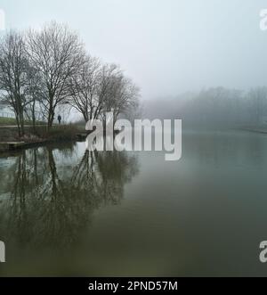 Waterside trees reflected in the boating lake, Corby, England, on a ...
