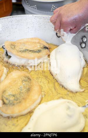 An adult Hispanic woman is frying battered poblano chilli pepper in a ...