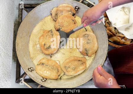 An adult Hispanic woman is frying battered poblano chilli peppers in a ...