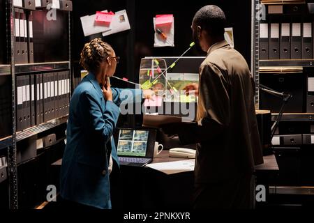 Detective partners analyzing crime scene photos on evidence board and ...