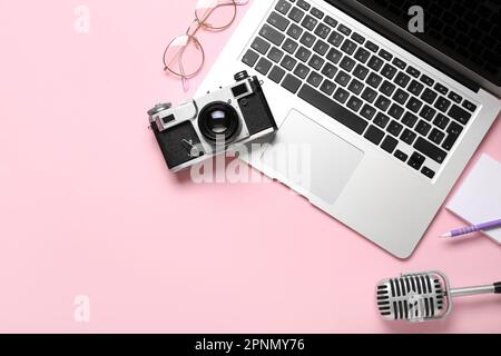 Laptop with photo camera, eyeglasses and microphone on pink background ...