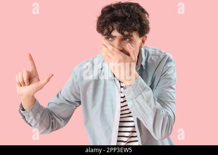 Laughing young man showing loser gesture and pointing at something on ...