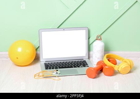 Laptop with sports equipment and headphones near green wall in gym ...