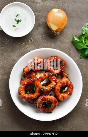 Bacon wrapped onion rings with sauce on plate over dark stone ...