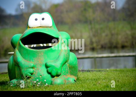 A well weathered, comical green frog shaped plastic rubbish bin in a ...