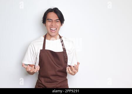 Portrait of annoyed Asian barista man in brown apron making angry hand ...
