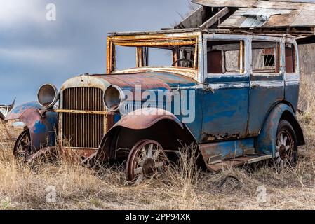 An abandoned vintage car with wooden spokes in a garden on the ...