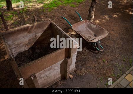 Still life with wheelbarrow standing near compost pit in a garden plot ...
