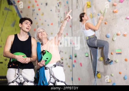 in gym, coach encourages client before climbing new difficult route and ...