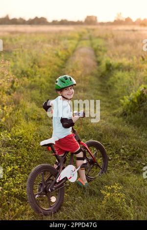 Rear view of boy wearing cycling helmet while riding bicycle on road ...