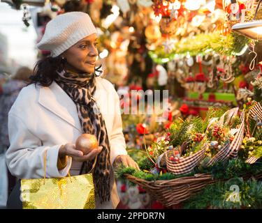 Woman is preparing for Christmas and choosing balls on the tree outdoor ...