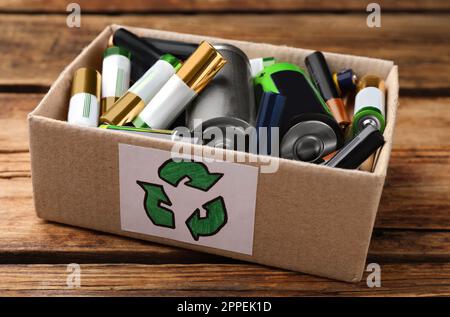 Used batteries in cardboard box with recycling symbol on wooden table ...