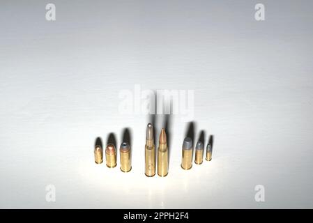 Bullets of different calibers standing on a white surface with dark ...