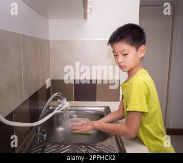 Kid boy washing dishes in the kitchen interior. Clean washed dishes, dishwashing liquid with ...