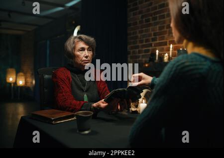 Old mature soothsayer holding divination tarot cards in front of client ...