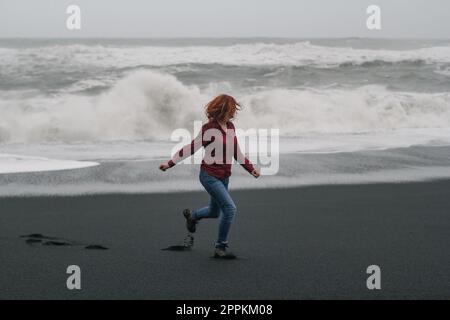 Redhead lady running along black beach scenic photography Stock Photo ...