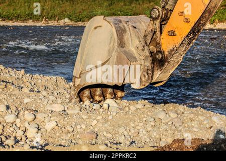 Digger (excavator machine) bucket digging stones ground by the river ...