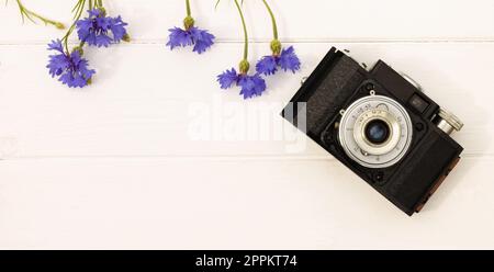 Retro vintage old camera with cornflowers and daisies on a white wooden ...