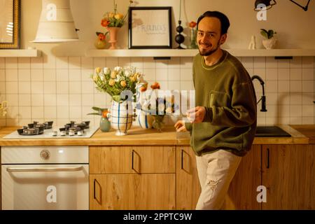Handsome man in a cozy kitchen speaks on the phone, jotting down notes ...
