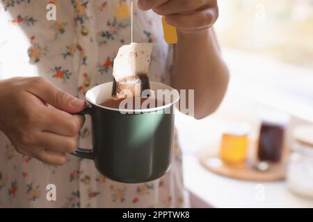 Woman taking tea bag out of cup at table indoors, closeup Stock Photo ...