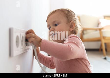 Cute baby playing with electrical socket and plug at home. Dangerous ...