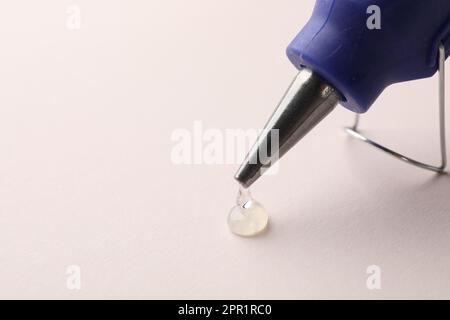 Melted glue dripping from hot gun on white table, closeup. Space for ...