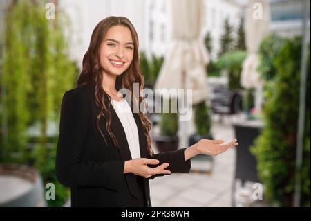 Portrait of hostess in uniform and blurred view of restaurant on sunny ...