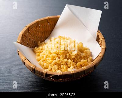 Tenkasu served in a colander placed against a wooden background. Image ...