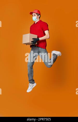 Delivery man in face mask holding cardboard box and jumping Stock Photo ...
