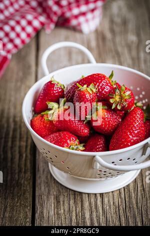 Strawberries in white colander placed on a rustic wooden background ...