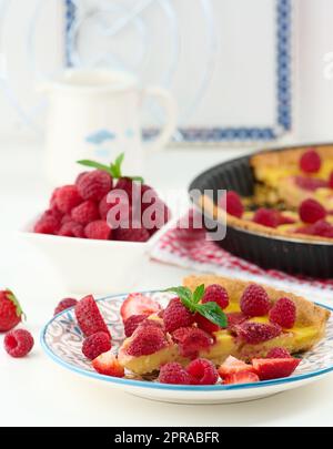 Round quiche with red strawberries and raspberries on a white table ...