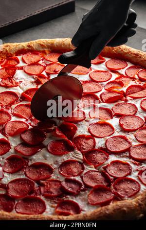 Cutting giant pepperoni pizza with special knife Stock Photo - Alamy