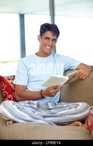 Sleep less, read more. a handsome young man sitting on his sofa while ...