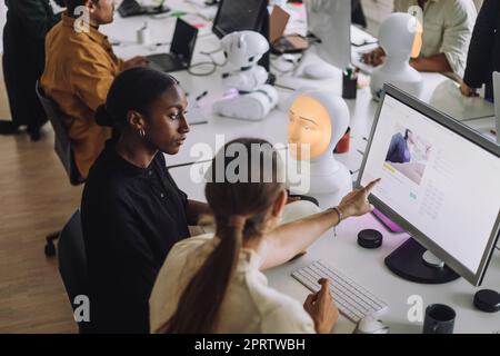 Multiracial female PhD students discussing over computer at desk in ...