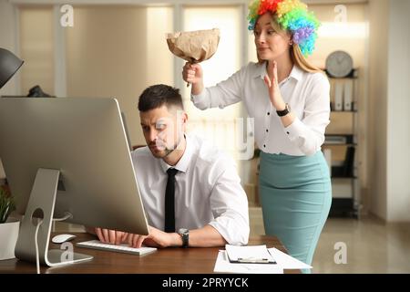 Young woman popping paper bag behind her colleague in office. Funny ...