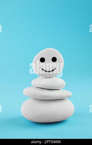 Stack of stones with drawn happy face, green leaves and water drops on ...