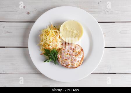 Fish cutlet with ham and melted cheese topping served with pickled ...