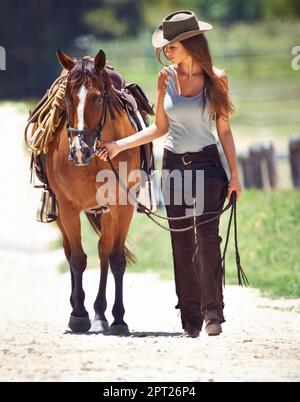 Loving the outdoors. A gorgeous cowgirl leading her horse along a country lane Stock Photo - Alamy