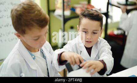 Adorable boys students using microscope writing notes at laboratory ...