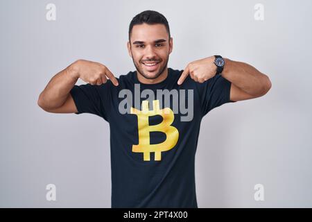 Young hispanic man wearing bitcoin t shirt smiling looking to the side ...