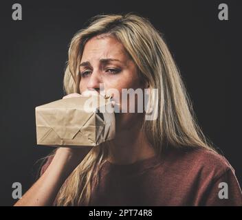 young woman breathing into paper bag while suffering from panic attack ...