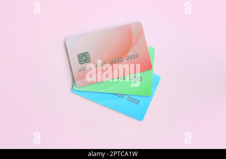 Three colored credit cards lay on a pastel pink background. The concept ...