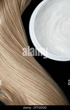 A strand of blond hair with hair balm on a black background. Close-up ...
