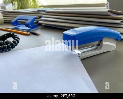 A large blue stapler for stapling paper lies next to the folders of ...