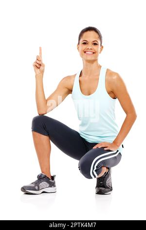 crouched woman looking at camera and pointing finger at ground on white ...