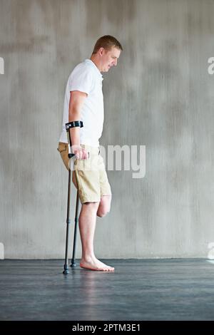 Getting back to normal. an young man with one leg walking on crutches ...