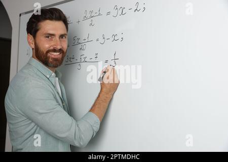 Happy teacher explaining mathematics at whiteboard in classroom Stock ...