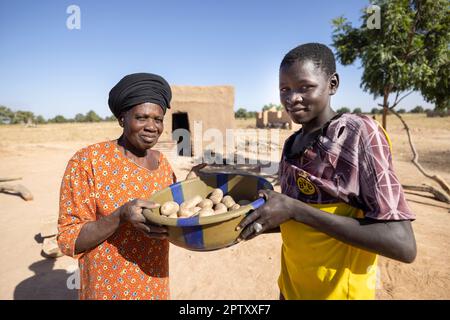 A male youth shares a basin of potatoes with an elderly woman neighbor ...