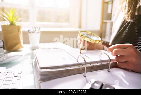 Woman using a magnifying glass to check the authenticity of a leather ...