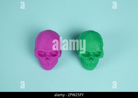 Two plastic skulls, one pink and one green, placed on a lace curtain ...